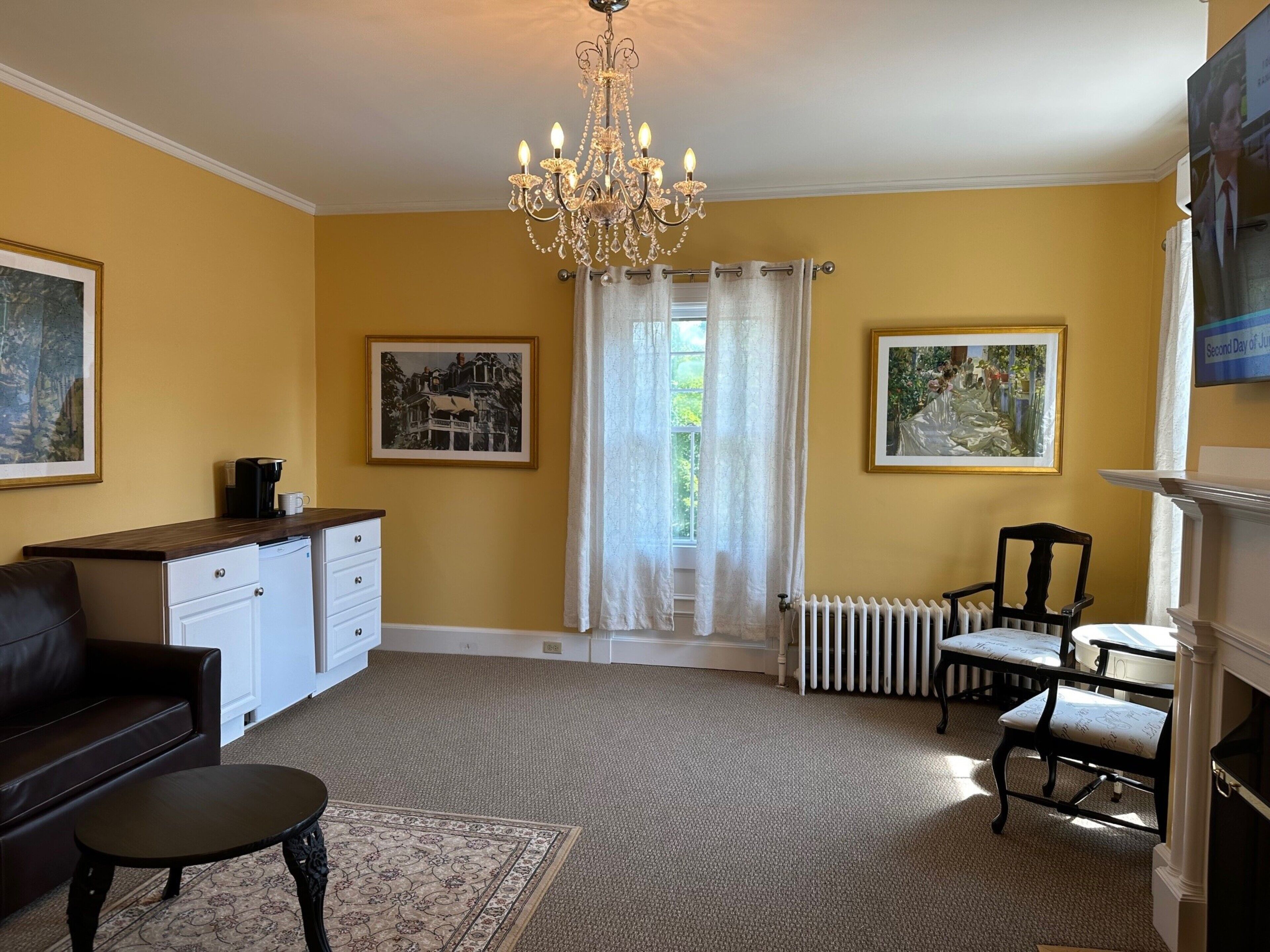 Uma sala de estar com um lustre, lareira, sofá, mesa de centro e radiador.