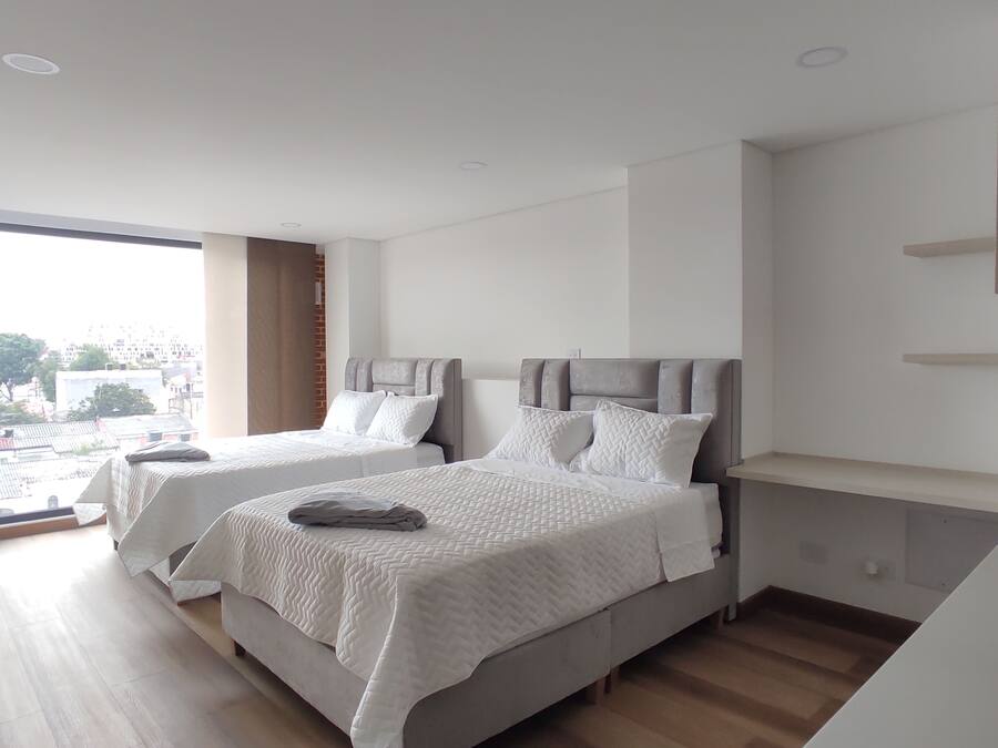 Quarto de hotel moderno com duas camas, uma janela grande e vista para a cidade.