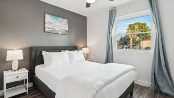 Quarto bem arrumado com cama, mesas de cabeceira, ventilador de teto e janela com cortinas.