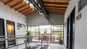 Um hall de hotel com teto alto, piso de terrazzo, escadaria e vista para a área externa.