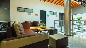 Um lobby moderno com teto alto, assentos de couro, uma pequena mesa com uma planta e uma porta de vidro que dá para o exterior.
