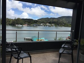 Varanda com duas cadeiras, vista para um lago, barcos e uma paisagem montanhosa.