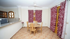 Uma área de jantar com uma mesa redonda e cadeiras, um ventilador de teto e cortinas estampadas.