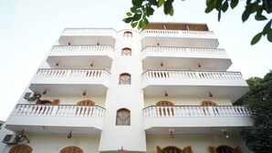 Um edifício de vários andares com paredes externas brancas, varandas com grades brancas e persianas de madeira nas janelas.