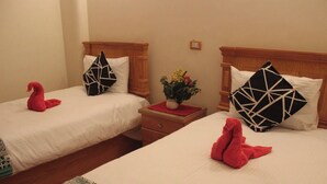 Duas camas de solteiro com cabeceiras de madeira, roupa de cama branca e toalhas em forma de flamingos vermelhos.
