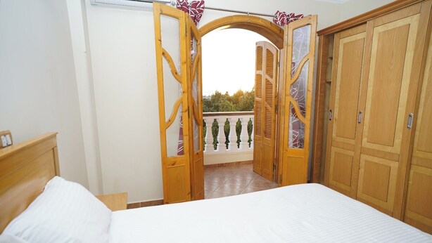 Quarto com cama, guarda-roupa de madeira e porta de varanda que dá para área externa.