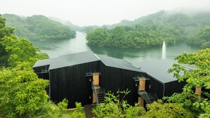 Um edifício moderno com fachada escura, rodeado por vegetação exuberante e um rio.