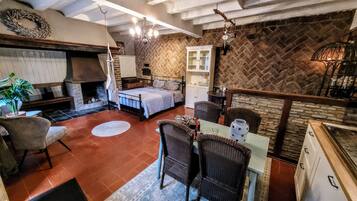 Um quarto acolhedor e rústico com lareira, uma cama, um espaço de refeições com cadeiras de vime e uma parede com padrão losango.