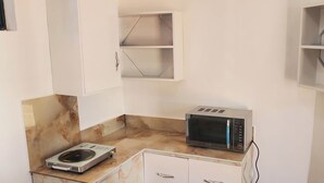 Cozinha compacta com micro-ondas, mini-geladeira e cafeteira, tudo sobre uma bancada de mármore.
