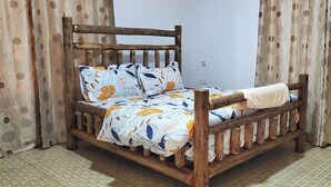 Uma cama de madeira com colcha florida e almofadas, cabeceira de madeira e cortinas com padrão circular.