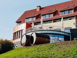 Um edifício moderno com telhado de telhas vermelhas, estruturas cilíndricas grandes e uma varanda com grades.