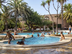 Uma área de piscina com várias piscinas, palmeiras e espreguiçadeiras.