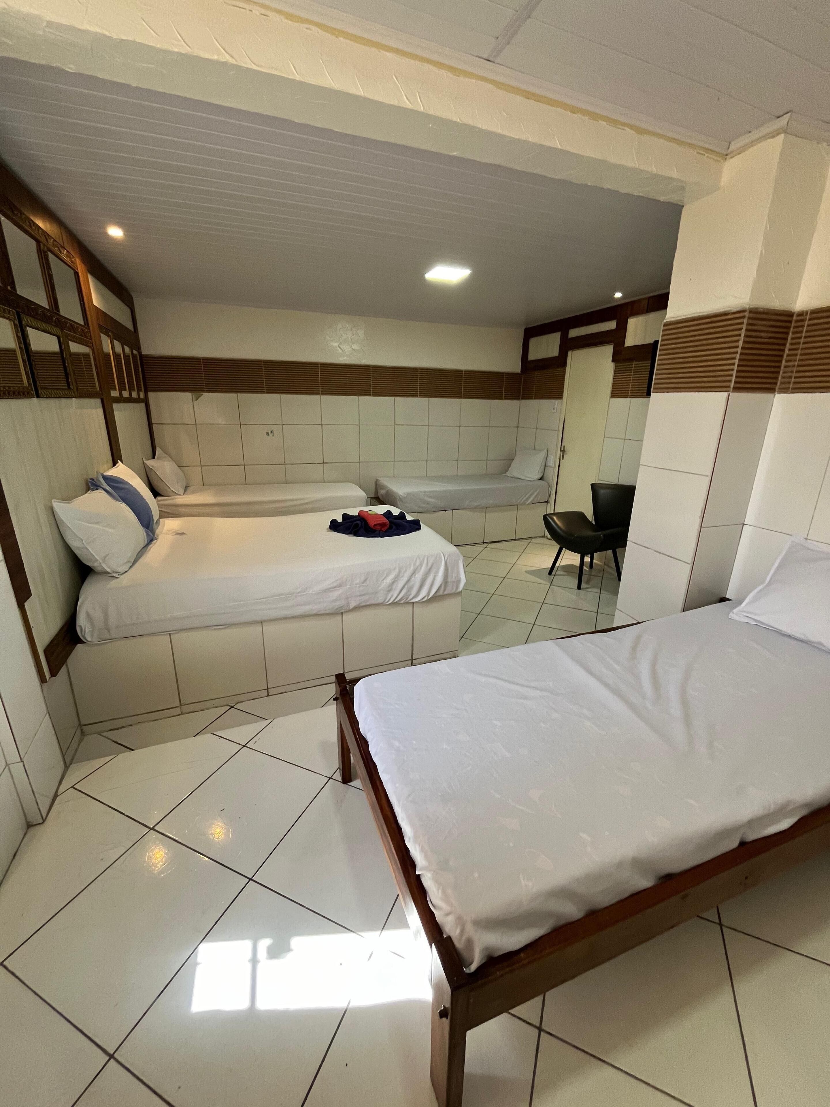 Quarto de hotel com duas camas de solteiro, uma mesinha e uma cadeira.