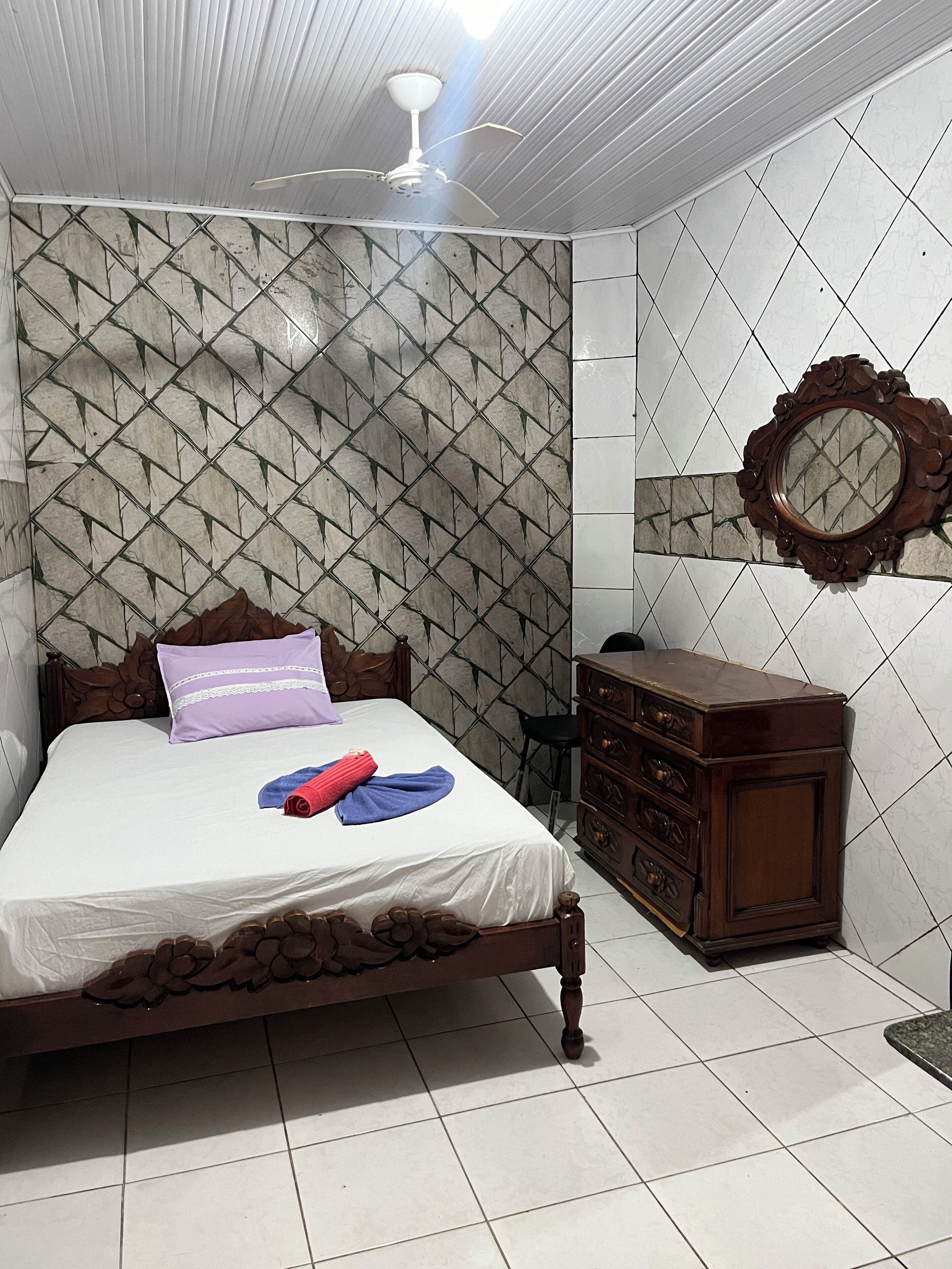 Quarto com cama, cômoda, espelho e ventilador de teto.