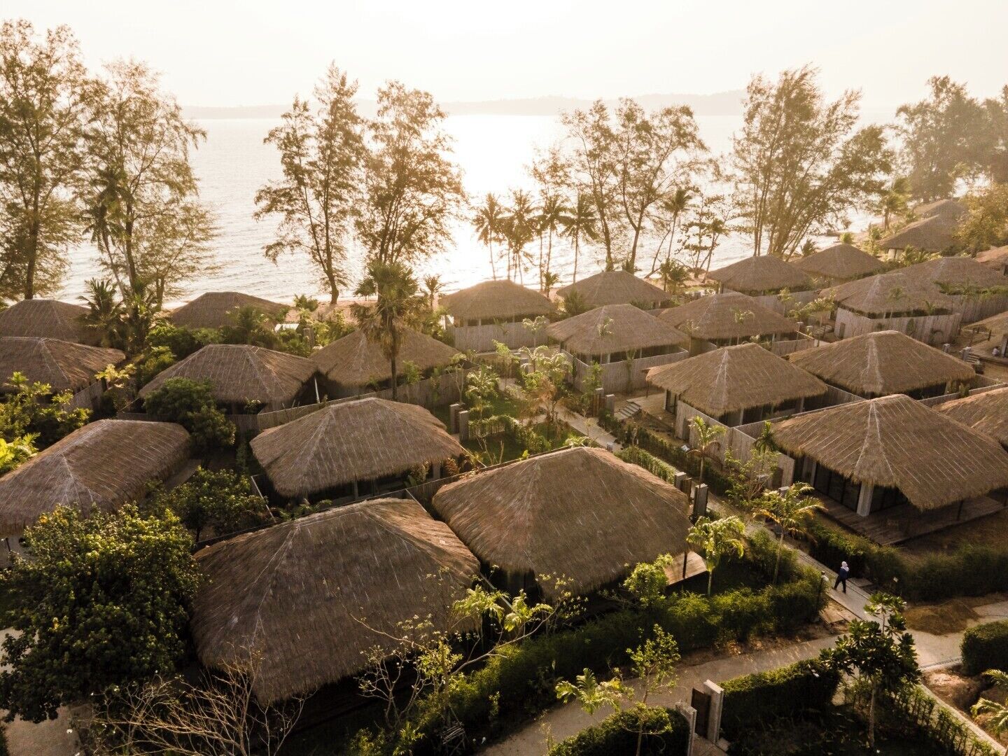 Um resort com cabanas de telhado de palha dispostas em fileiras, com vista para um corpo de água.
