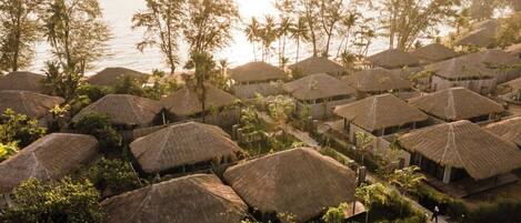 Um resort com cabanas de telhado de palha dispostas em fileiras, com vista para um corpo de água.
