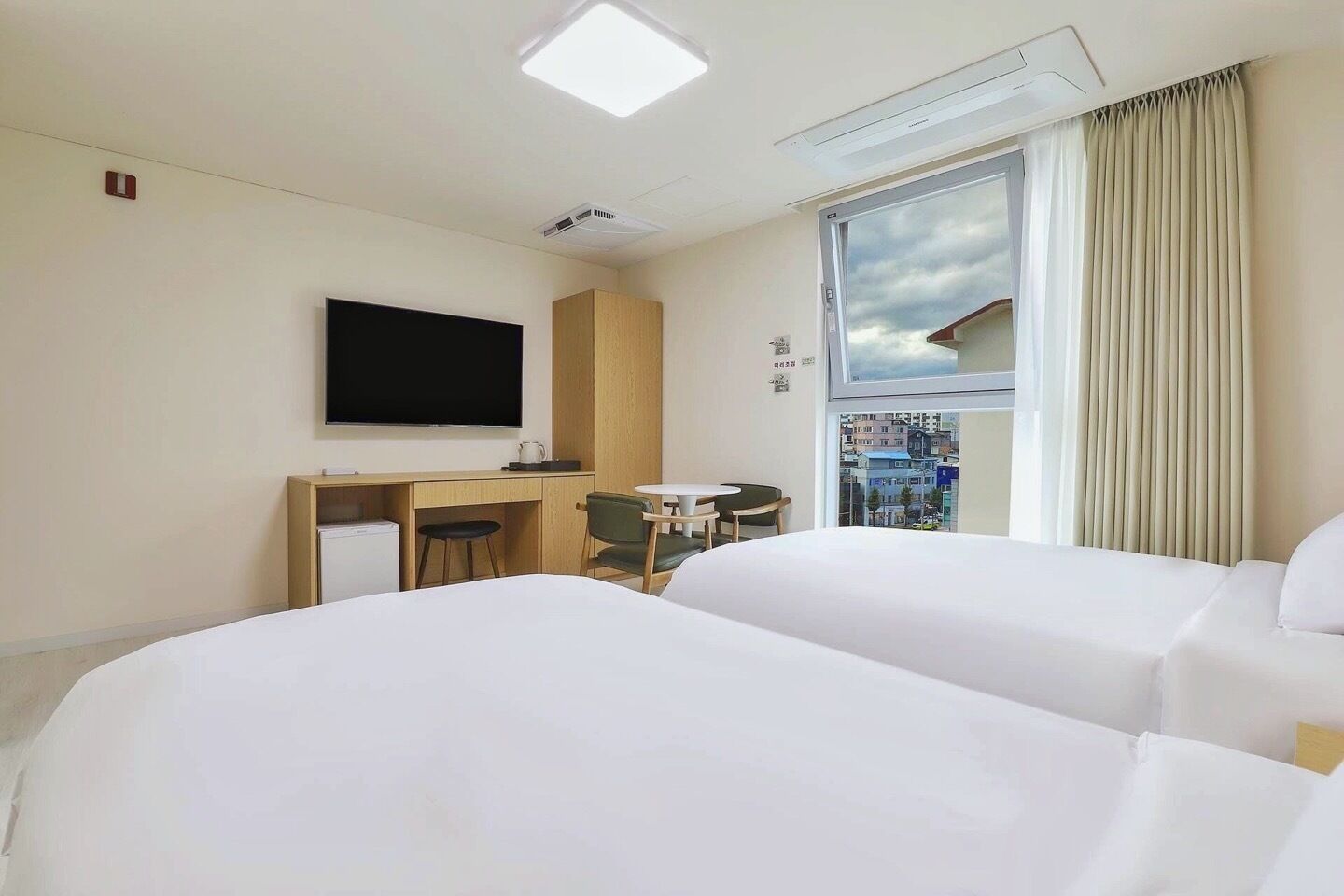Quarto de hotel com duas camas, uma mesa, uma cadeira, televisão e uma janela com cortinas.