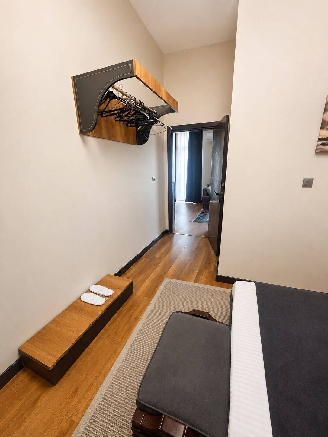 Quarto de hotel moderno com uma cama, um banco de madeira, uma mesinha e um espelho fixado na parede.