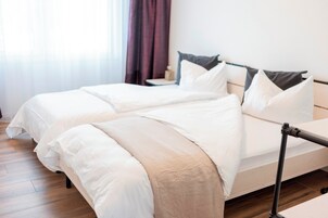 Quarto de hotel com duas camas, uma mesinha de cabeceira e uma janela com cortinas.