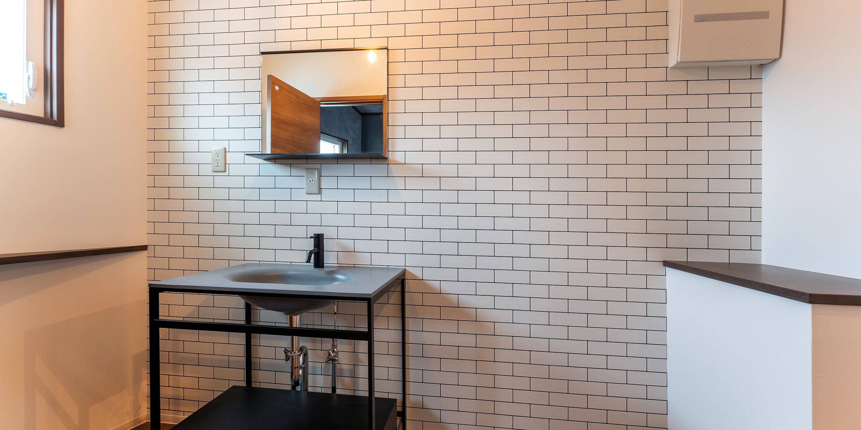 Casa de banho com parede revestida de azulejos brancos, espelho com moldura preta, lavatório moderno e armário preto.
