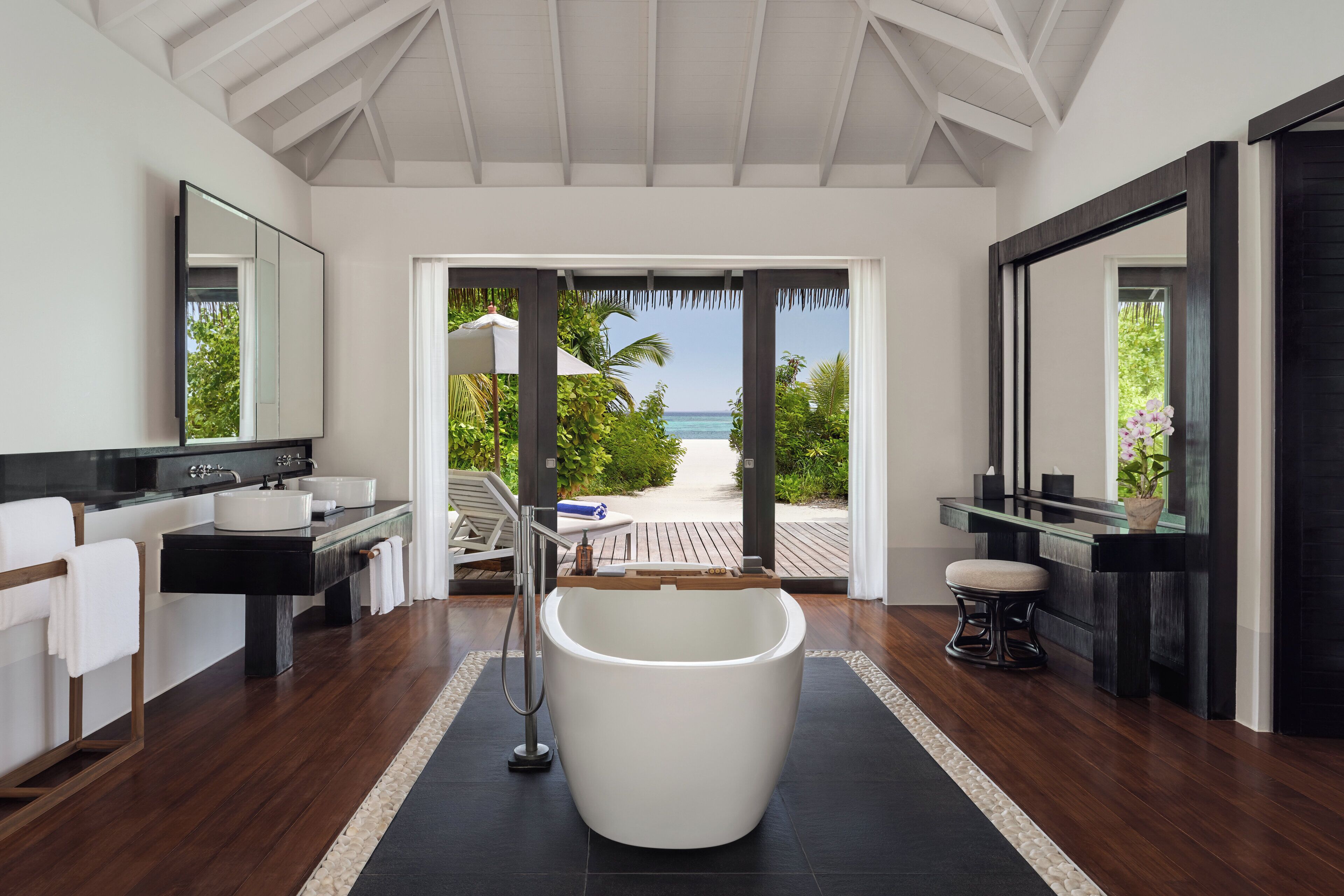 Uma casa de banho moderna com banheira, um espelho grande e vista para a praia.