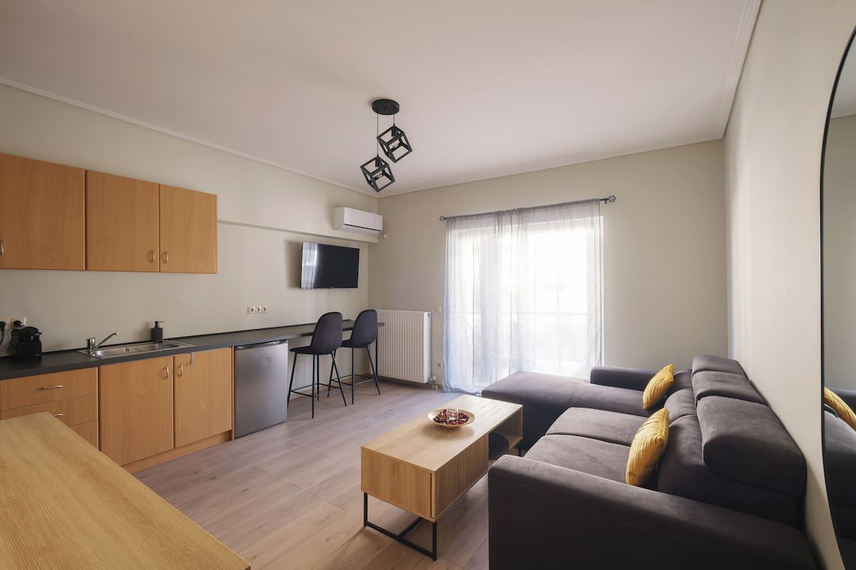 Uma sala de estar moderna com um sofá, uma mesa de centro e uma área de cozinha com armários e uma televisão.