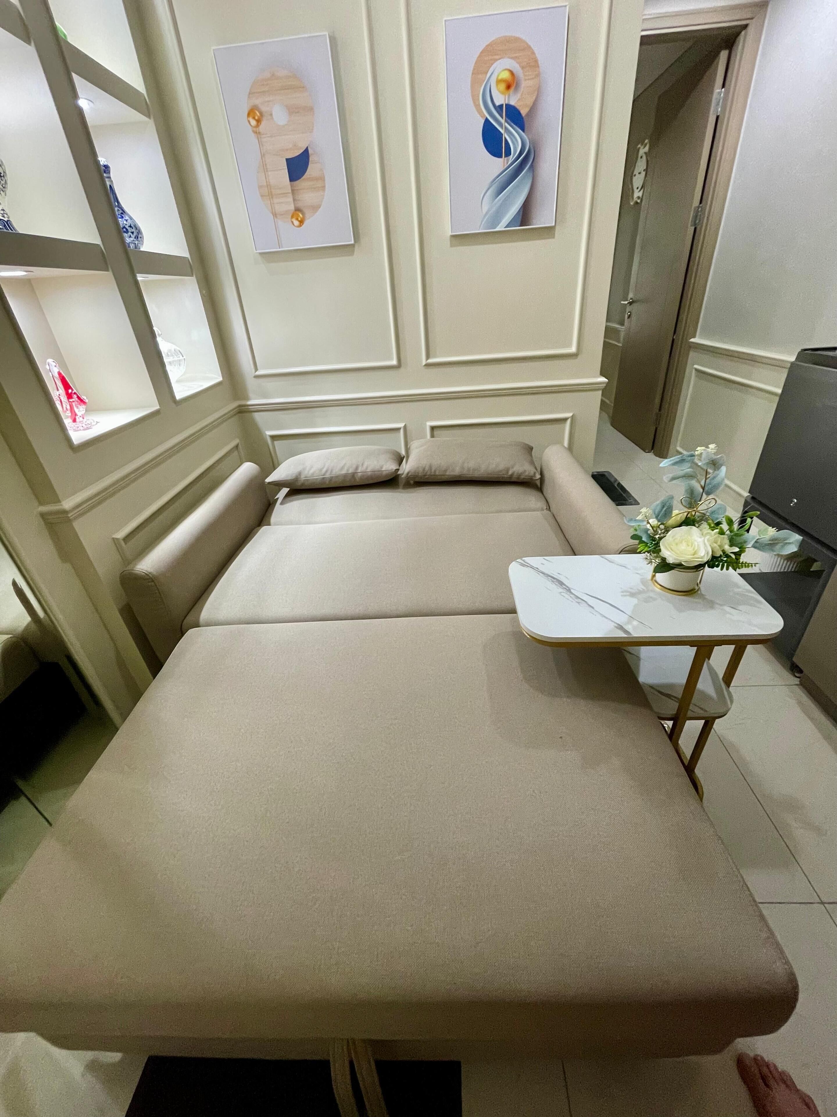 Um quarto com uma cama, uma mesinha com um vaso e obras de arte na parede.