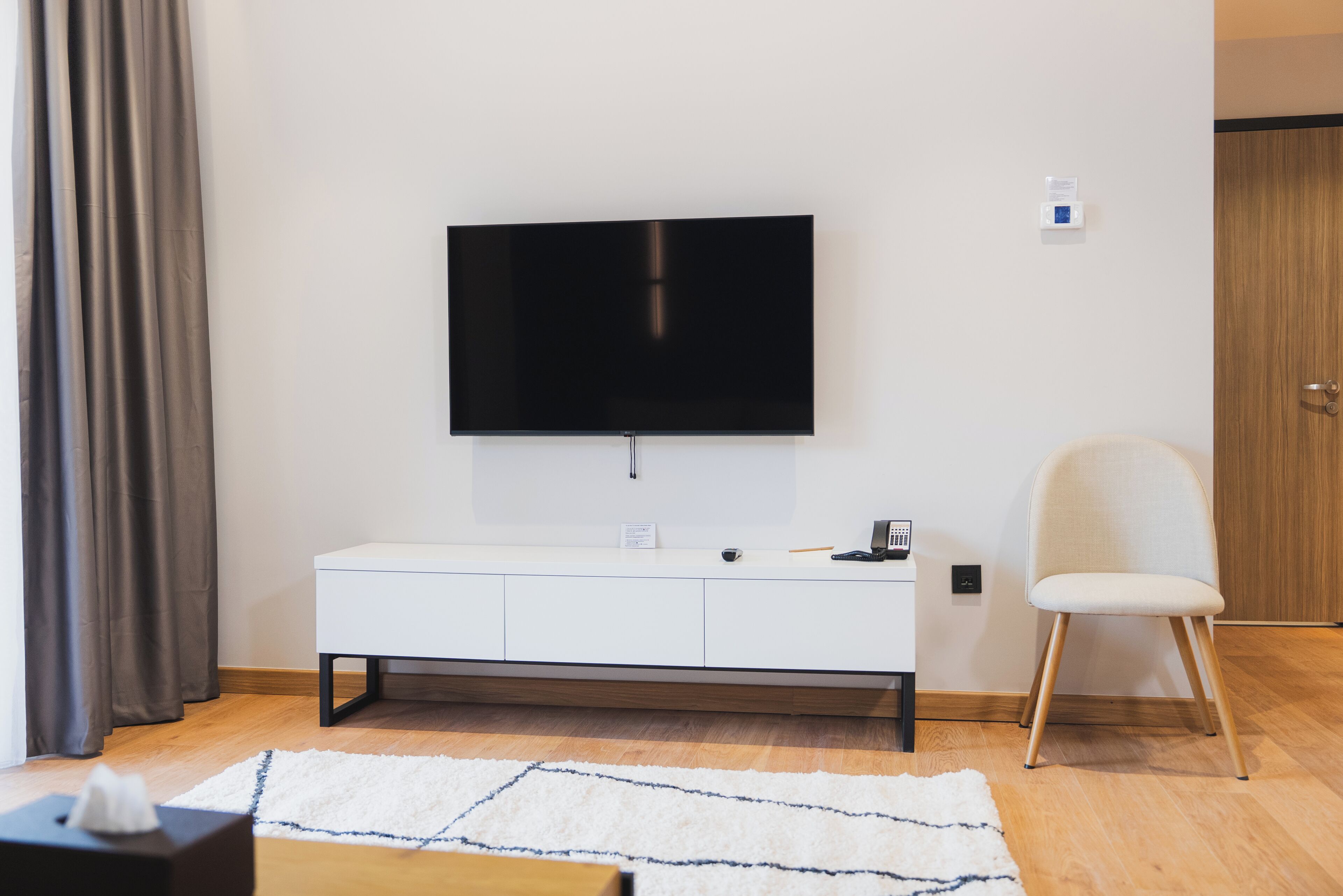 Uma sala de estar moderna com televisão de tela plana na parede, um sofá branco, piso de madeira e um tapete branco.