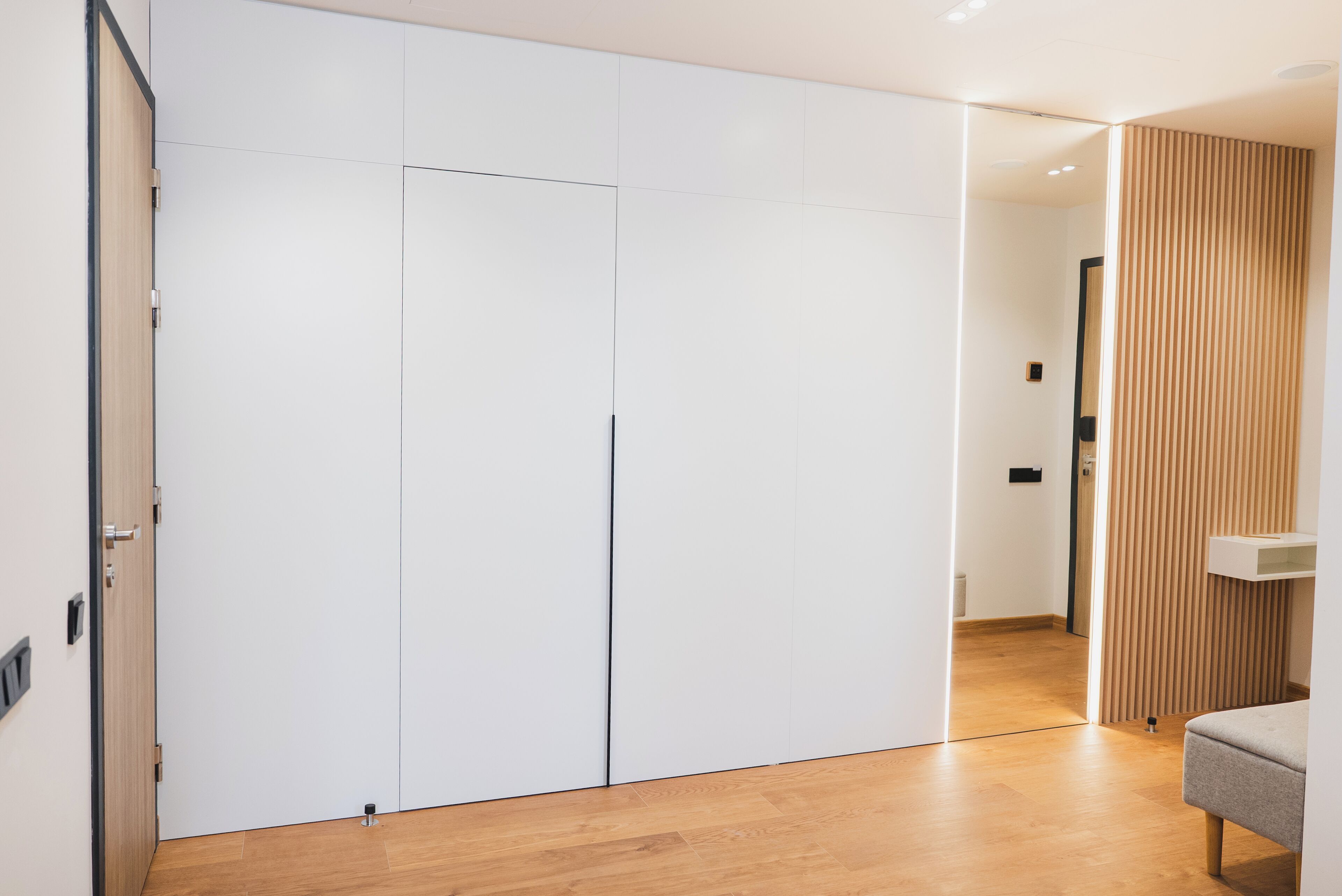 Quarto moderno com armário branco de correr, soalho de madeira e cama em tons neutros.