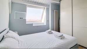 Quarto de hotel com cama, janela, radiador e guarda-roupa.