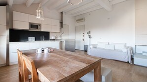 Um espaço de estar moderno e minimalista, com uma mesa de jantar de madeira, sofás brancos e uma cozinha com armários brancos e micro-ondas.