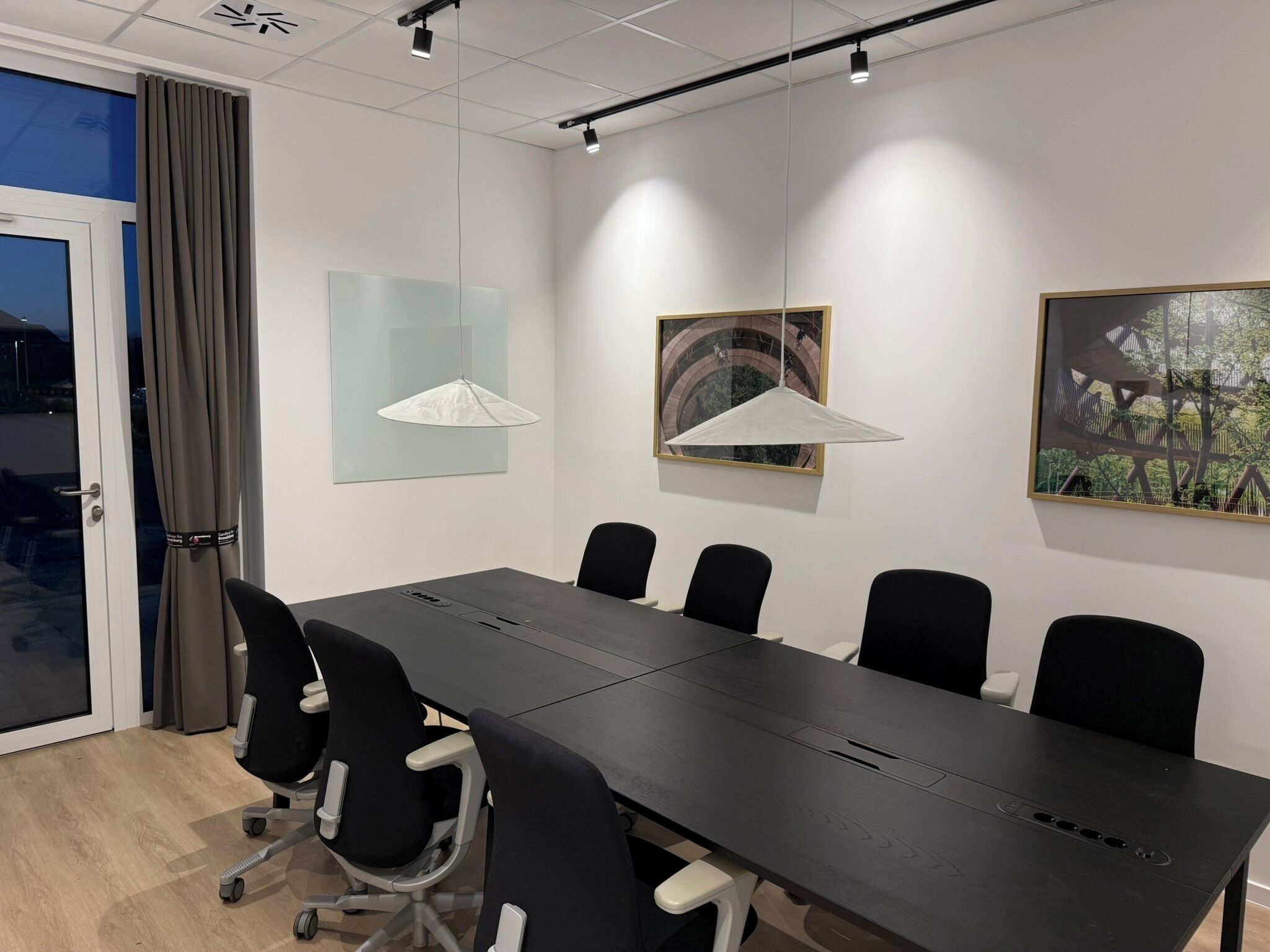 Uma sala de conferência com uma mesa comprida, seis cadeiras e duas luminárias pendentes.