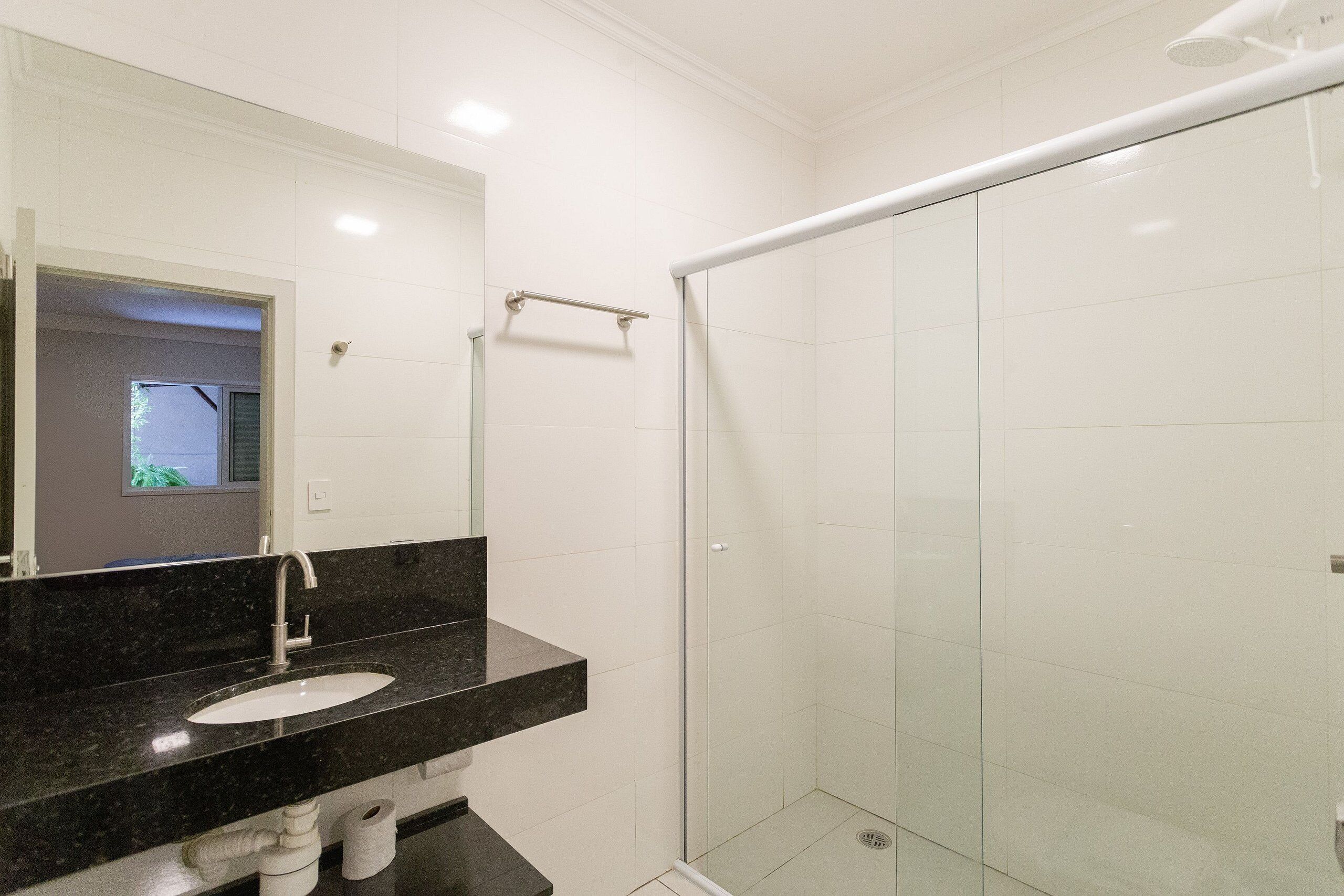 Uma casa de banho moderna com bancada de granito preto, lavatório branco e cabine de chuveiro envidraçada.