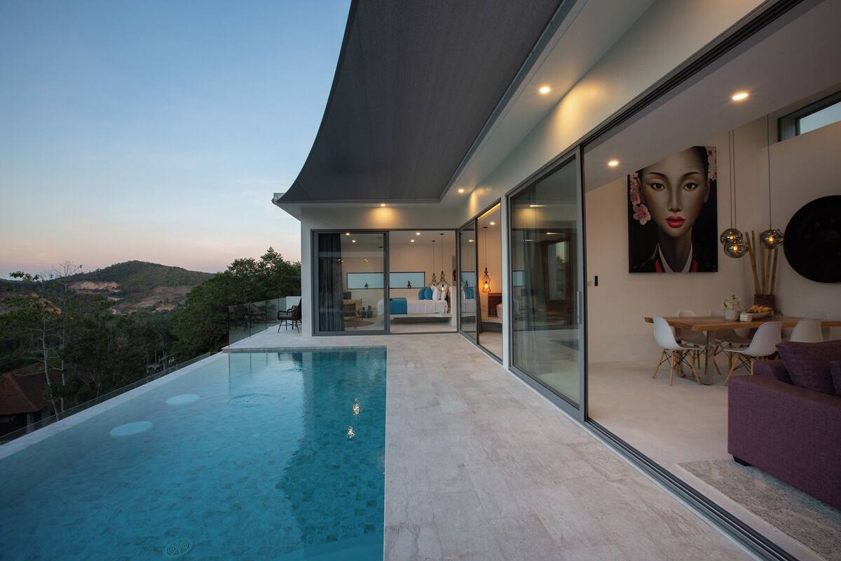 Uma casa moderna com uma grande porta de vidro que dá para uma sala de jantar, uma piscina e vista para as colinas.