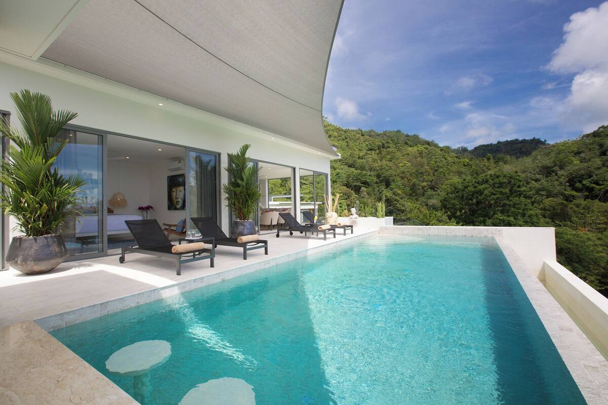 Uma área de piscina moderna ao ar livre, com espreguiçadeiras e plantas em vasos, com vista para uma encosta.
