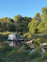 Estrutura em cúpula geodésica com deck e área de estar, localizada à beira de águas calmas e rodeada por vegetação.
