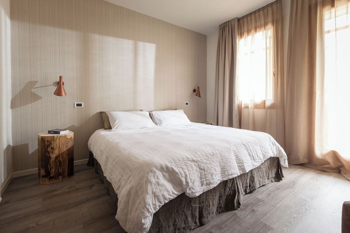 Quarto com cama grande, piso de madeira e janela com cortinas.