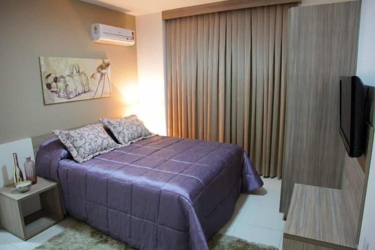 Quarto com cama, mesa de cabeceira, televisão e um quadro na parede.