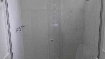 Um chuveiro pequeno e fechado, com porta de vidro, um vaso sanitário e uma toalha pendurada em uma barra de metal.