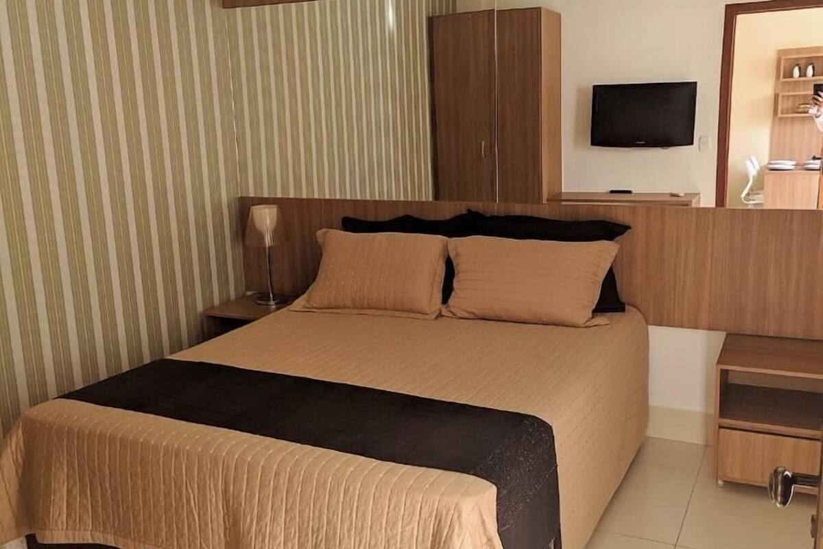Quarto moderno com cama grande, televisão e guarda-roupa de madeira.