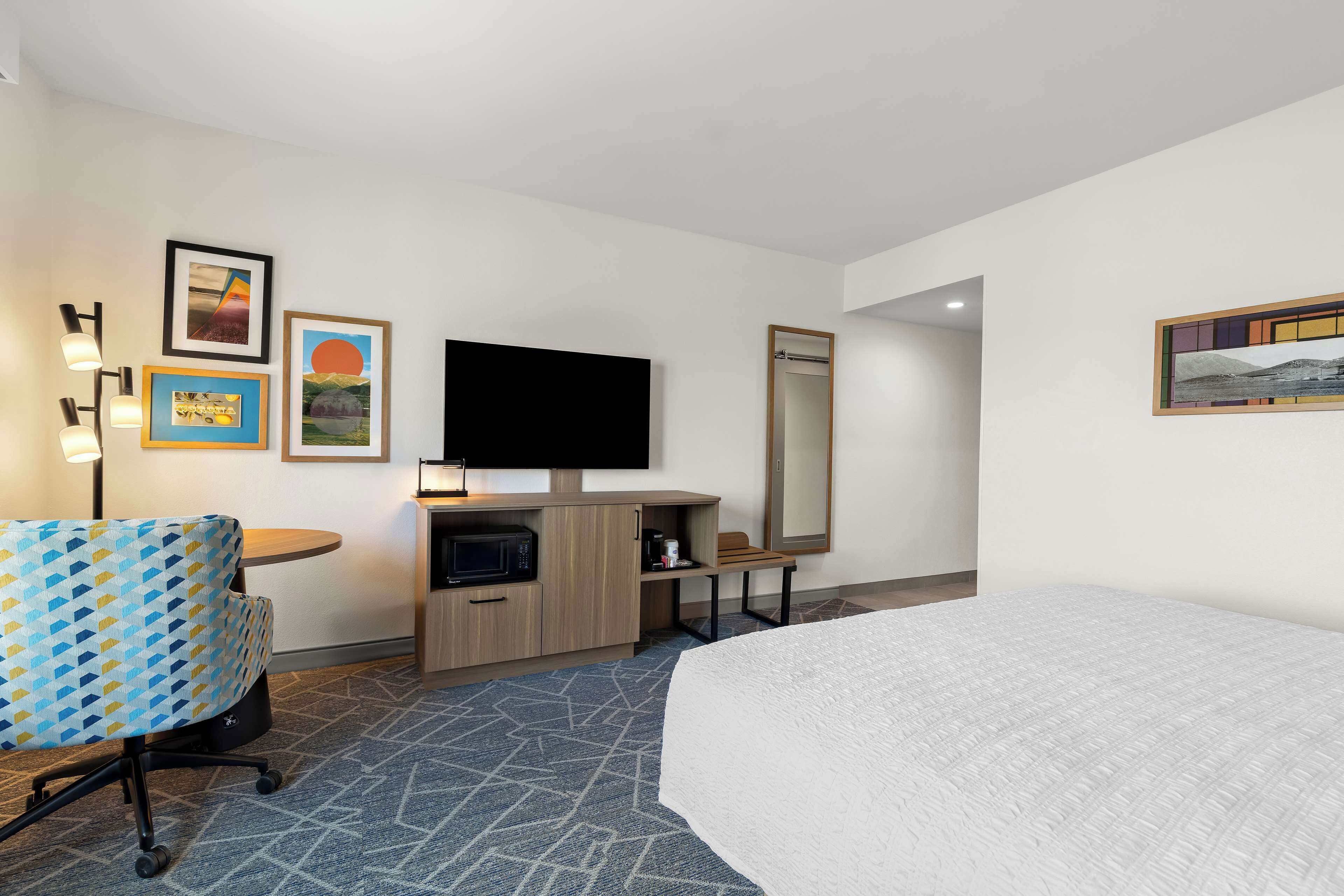 Quarto de hotel com cama, escrivaninha, televisão de tela plana, cadeira, micro-ondas e quadros na parede.