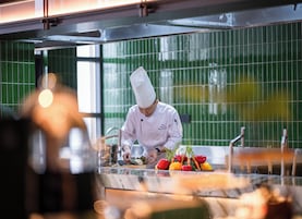 Um chef em uma cozinha profissional com paredes de azulejos verdes e equipamentos de aço inoxidável.