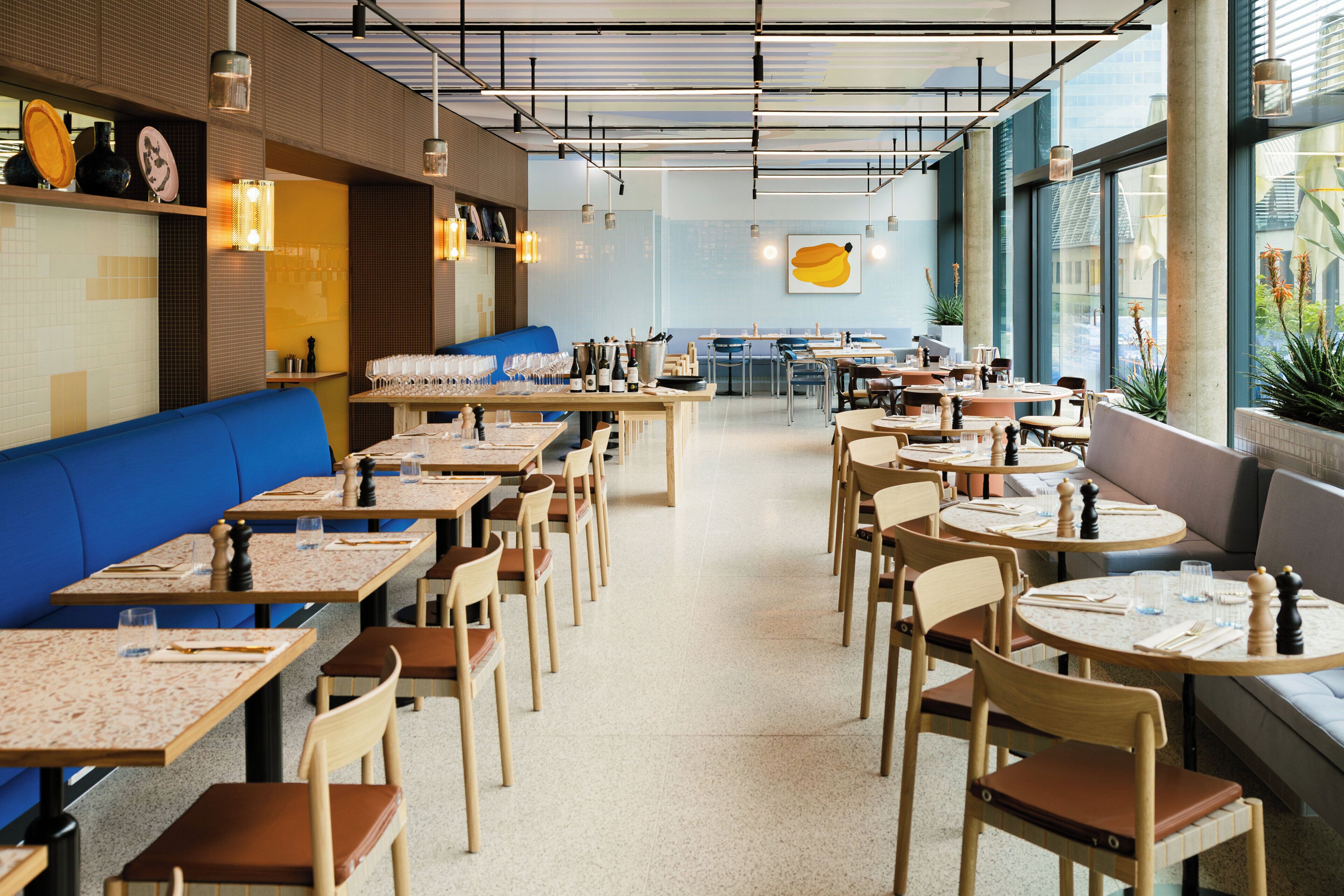 Interior moderno de restaurante com diversas opções de assentos, incluindo cabines e mesas, área de bar visível e grandes janelas que oferecem vistas.