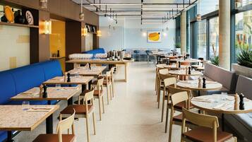 Interior moderno de restaurante com diversas opções de assentos, incluindo cabines e mesas, área de bar visível e grandes janelas que oferecem vistas.