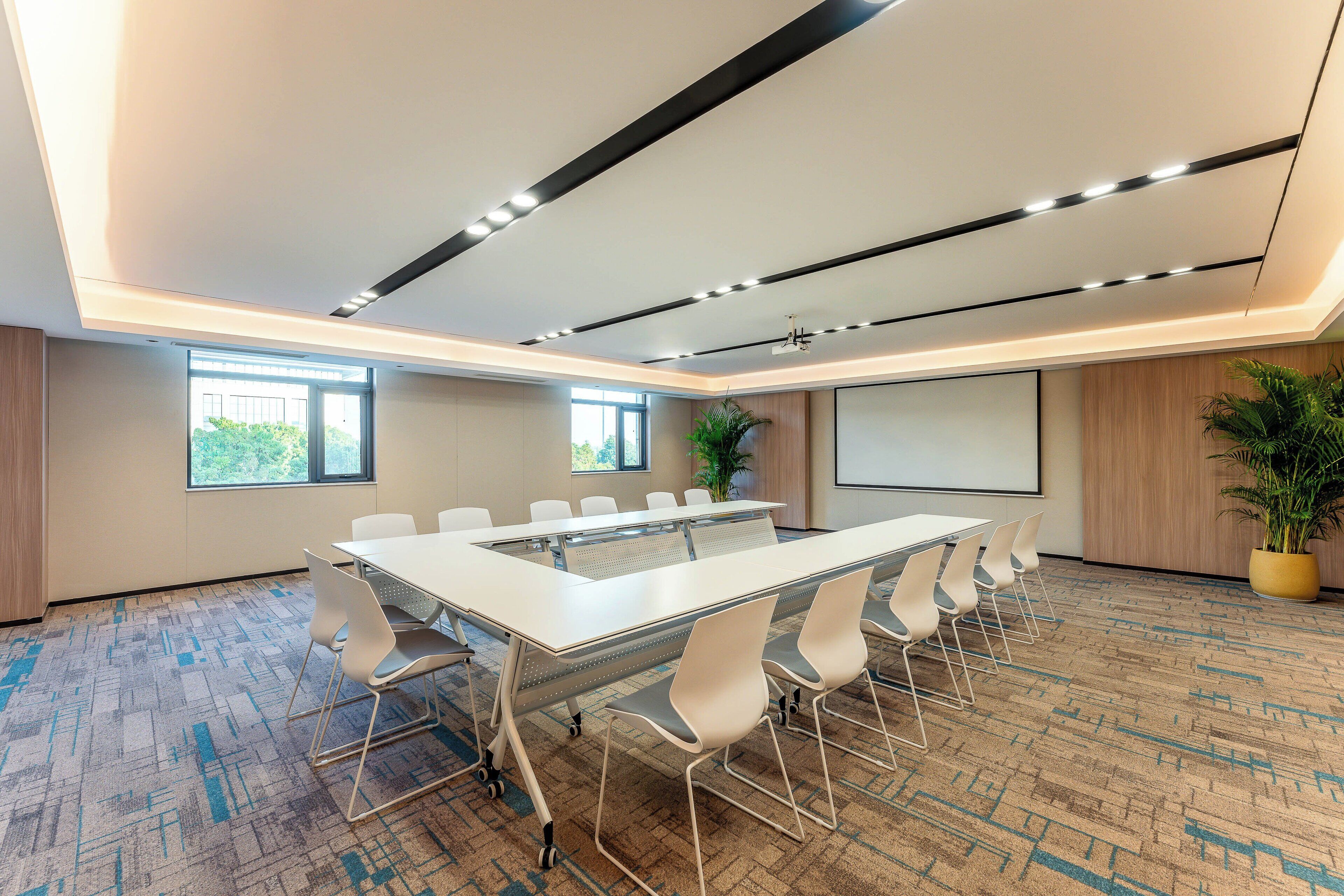 Uma sala de conferências com uma mesa comprida, cadeiras, um projetor e uma janela grande.