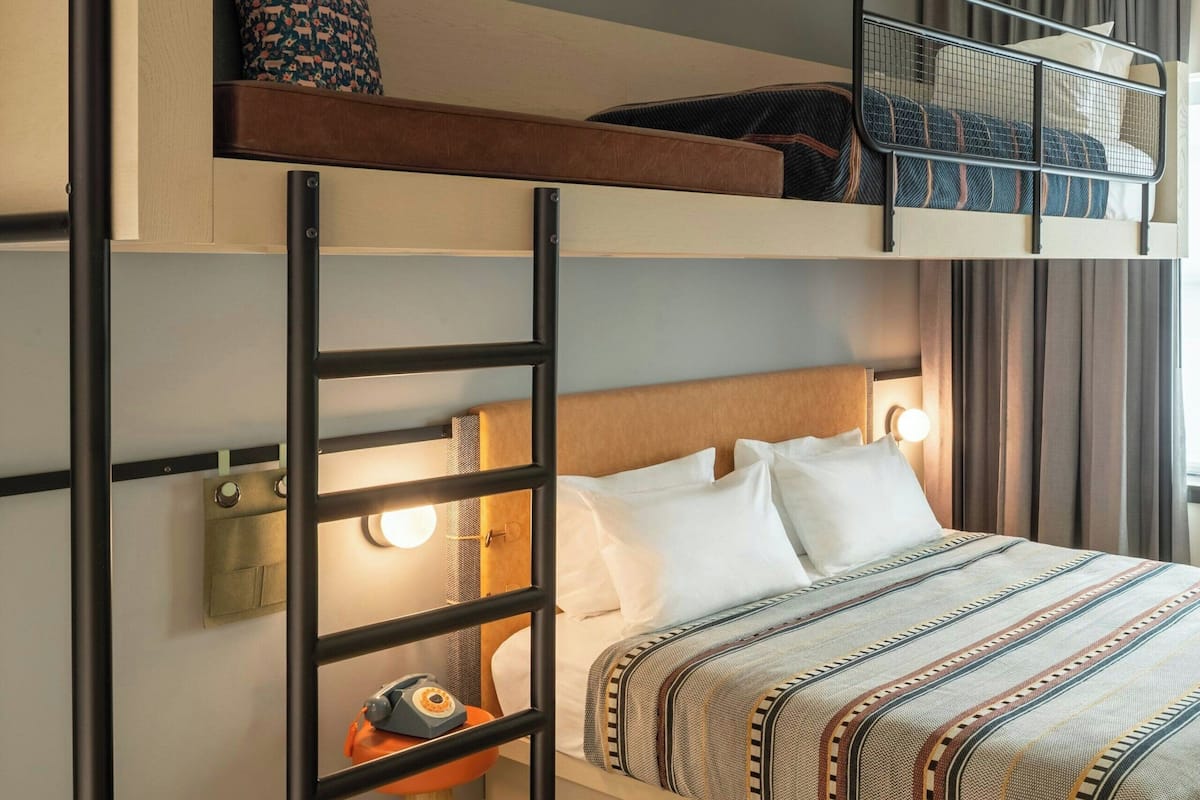 Quarto com beliche, mesa de cabeceira com abajur e colcha estampada.