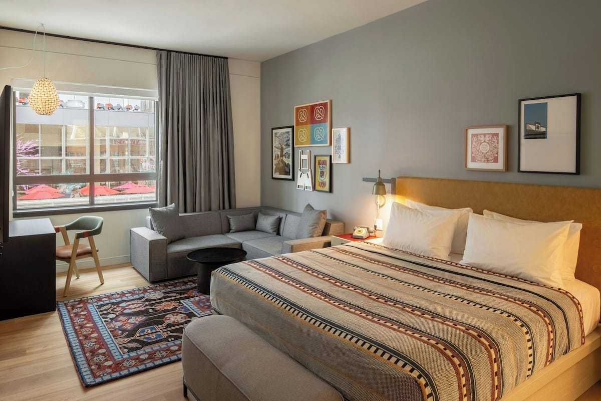 Quarto de hotel moderno com uma cama grande, um sofá, uma escrivaninha e uma janela com cortinas.