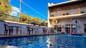 Piscina com espreguiçadeiras e um edifício com varanda.