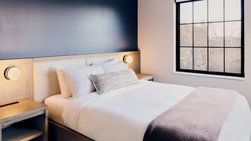 Quarto de hotel moderno com uma cama grande, uma mesinha de cabeceira e uma janela com vista para edifícios.