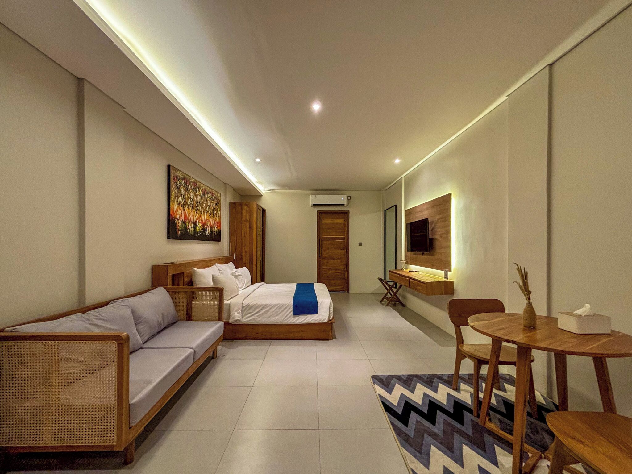 Quarto de hotel moderno com sofá, cama, escrivaninha e mesa de jantar.